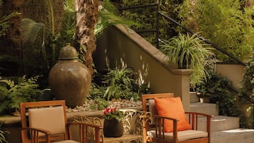 Uma área externa com assentos, duas cadeiras de madeira, uma mesa e um candeeiro decorativo.