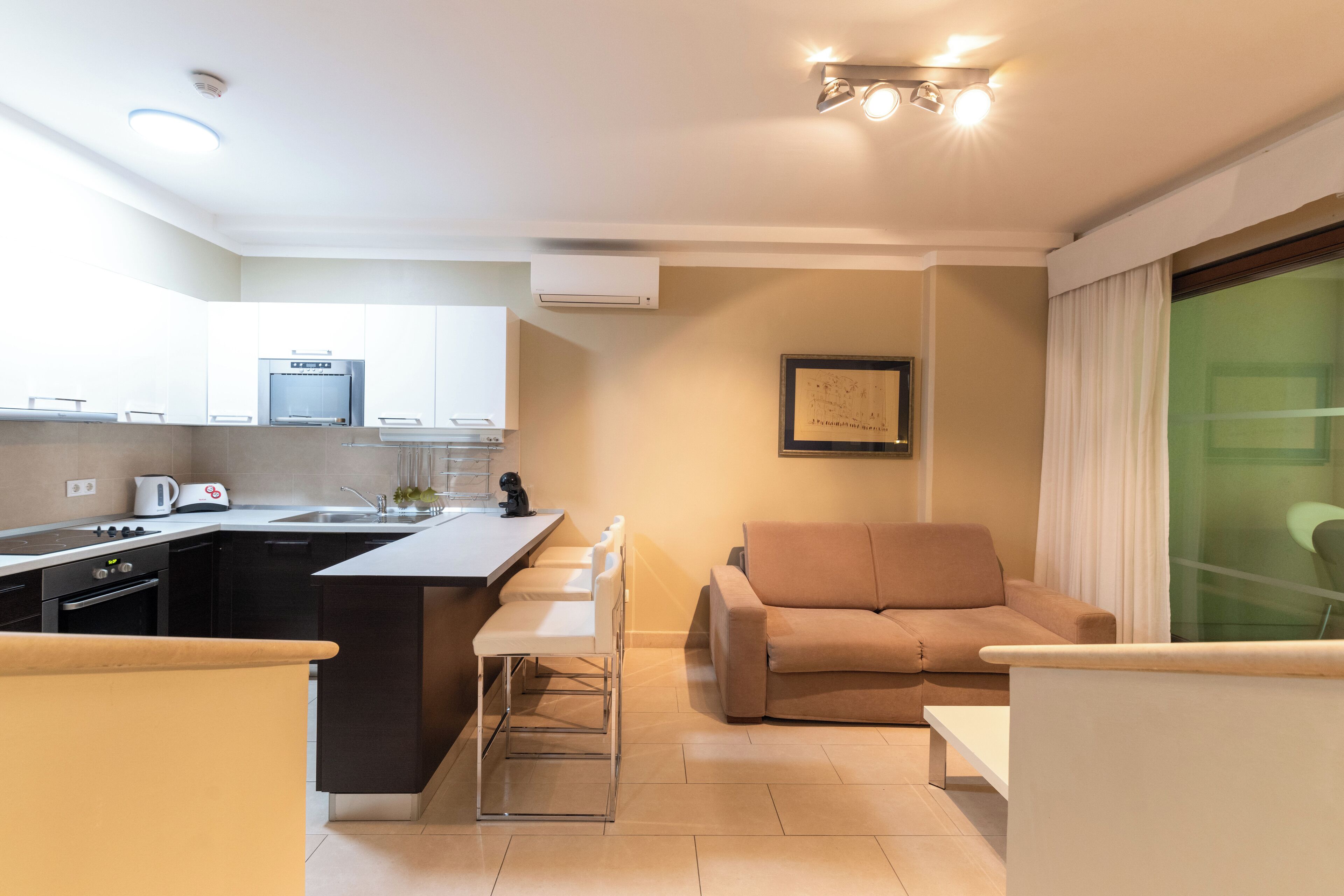 Uma cozinha moderna com uma ilha central, uma área de jantar com banquetas, um sofá e um quadro na parede.