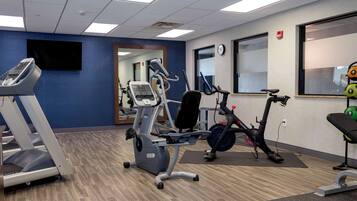 Academia com máquinas de cardio, espelho e relógio na parede.
