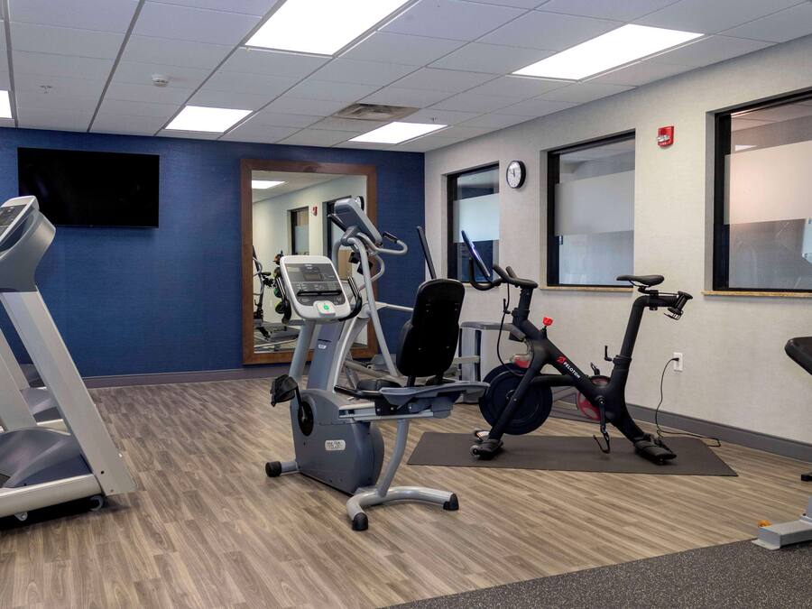 Academia com máquinas de cardio, espelho e relógio na parede.