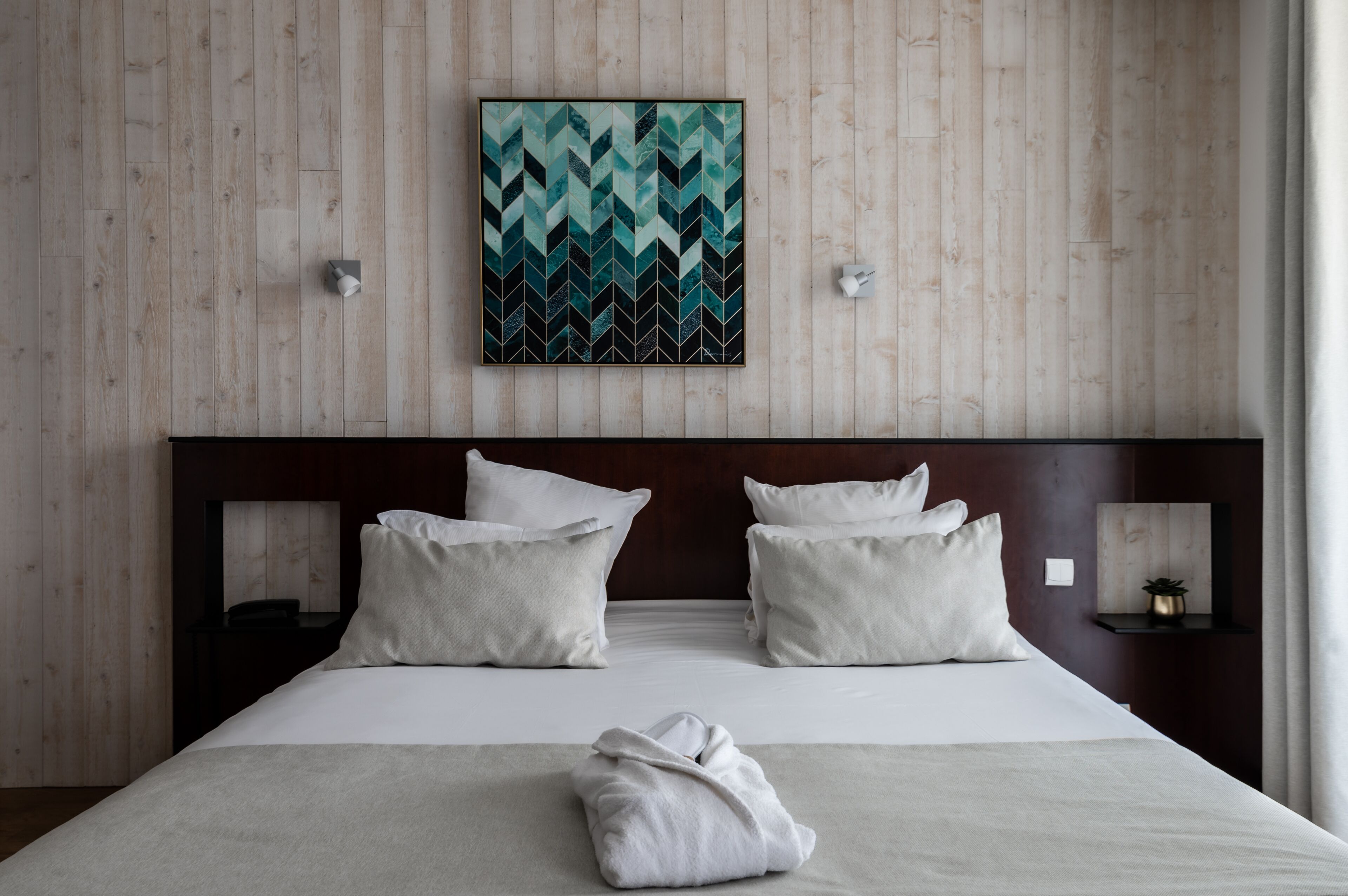 Cama bem arrumada com lençóis e almofadas brancos, cabeceira de madeira e uma obra de arte na parede.