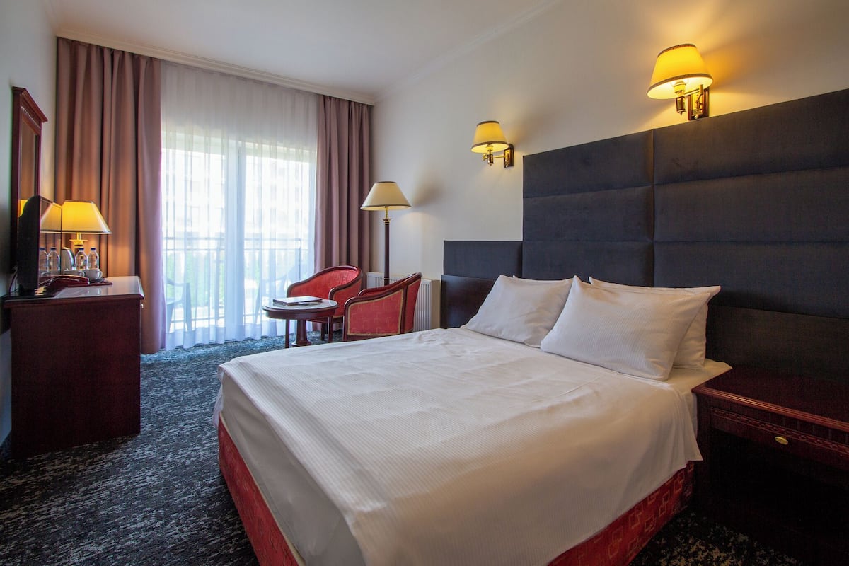 Quarto de hotel com uma cama grande, uma escrivaninha com abajur, uma cadeira e duas luminárias de parede.