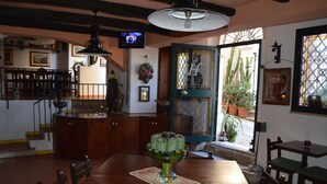 Uma mesa de jantar de madeira com um arranjo verde, uma escada com corrimão e uma porta com painel de vidro.