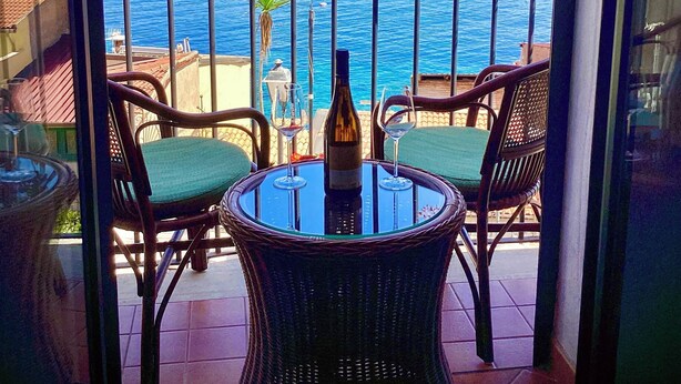 Uma varanda com uma mesa, duas cadeiras e uma garrafa de vinho.