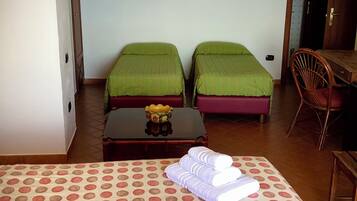 Quarto de hotel com duas camas de solteiro, uma mesa de madeira com um vaso, uma cadeira e uma cama grande com cobertura estampada de bolinhas.