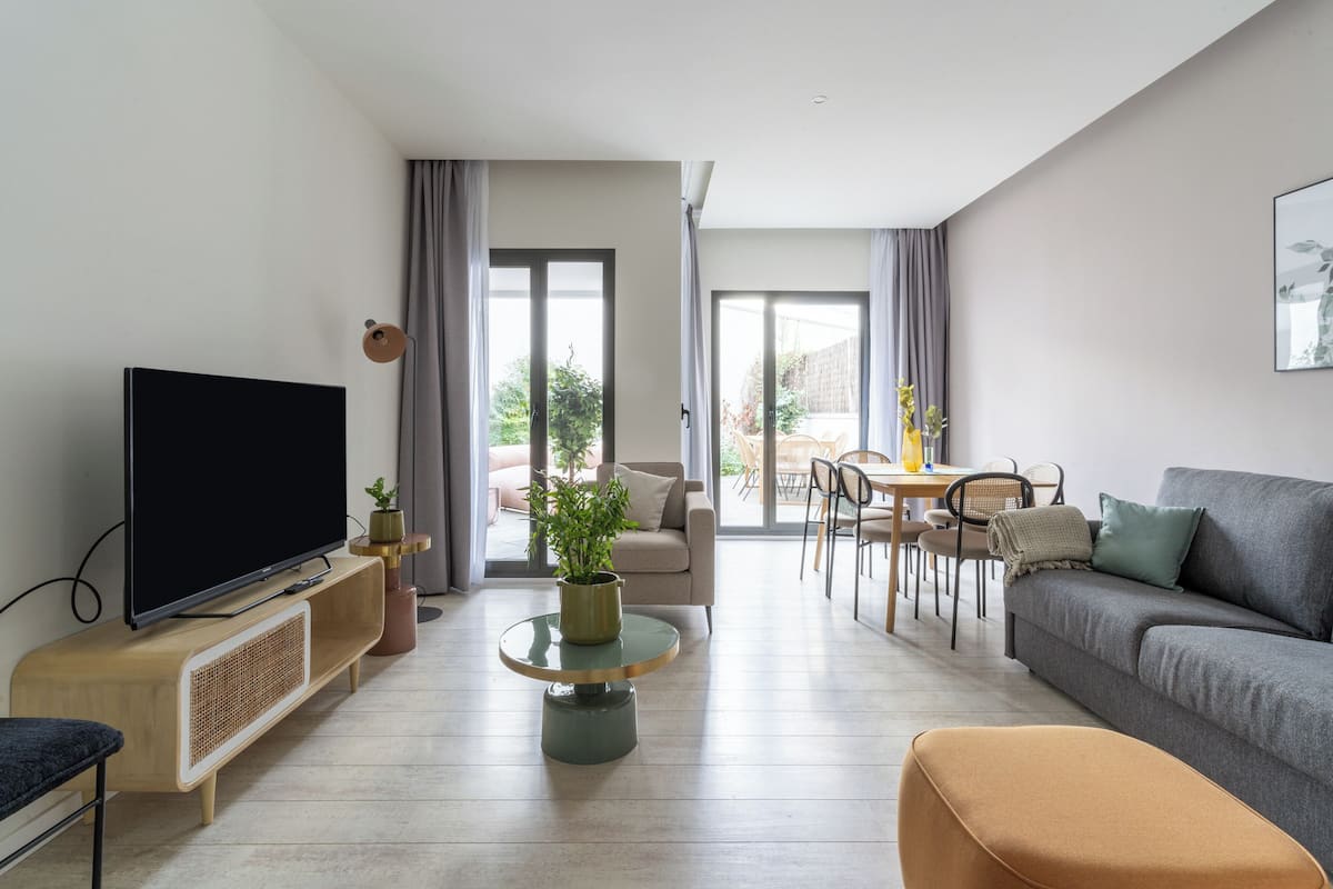 Uma sala de estar moderna com uma TV de tela plana, uma mesa de centro redonda, um sofá e uma área de jantar com cadeiras e uma mesa.