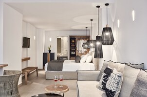 Quarto de hotel moderno com cama, sofá e área de refeições com mesa e cadeiras.