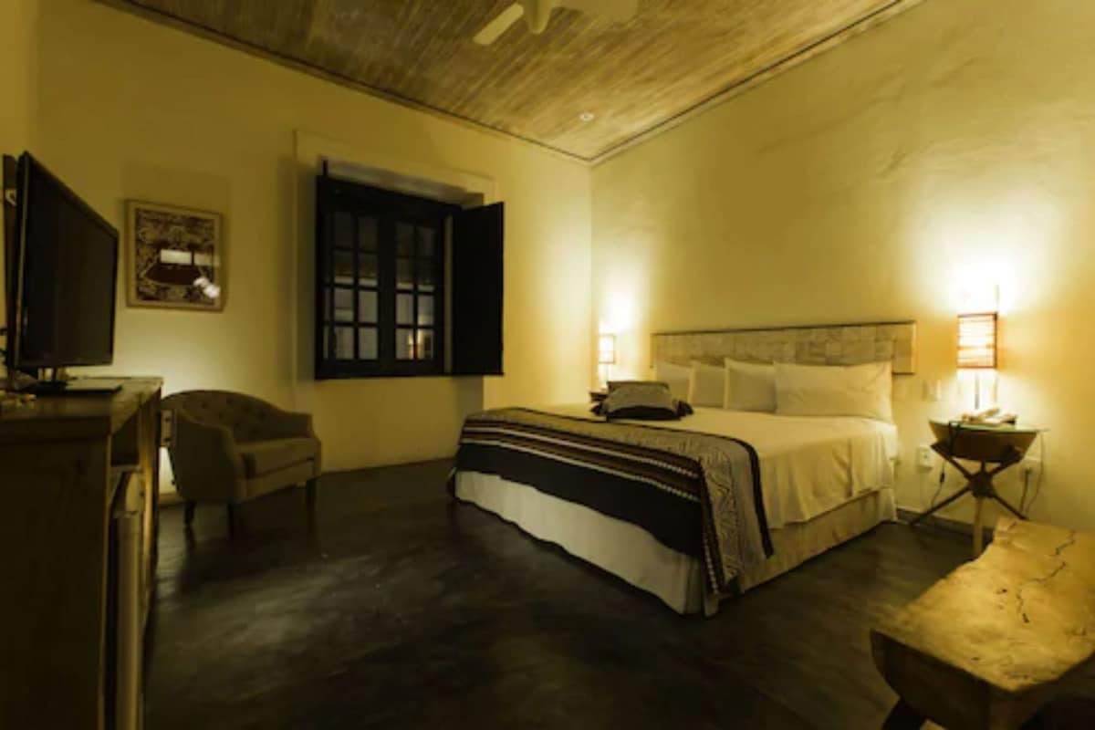 Quarto com cama, mesa de cabeceira, luminária, cadeira e televisão.