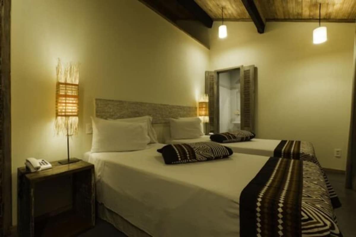 Quarto de hotel com duas camas, teto de madeira e abajures.