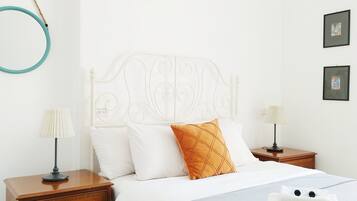 Um quarto bem organizado com uma cama, duas mesas de cabeceira, um criado-mudo, uma luminária circular na parede e um tapete estampado.