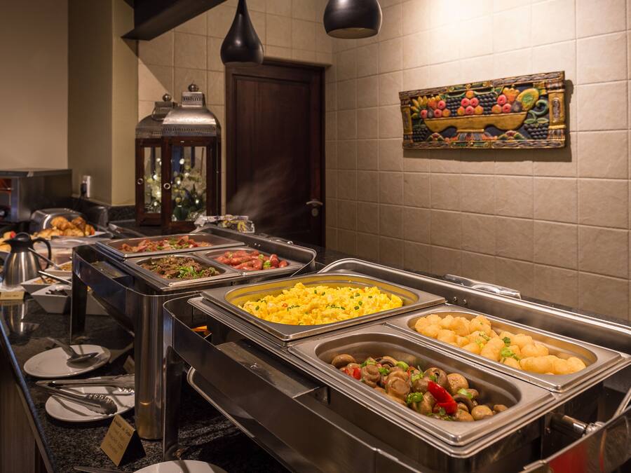 Buffet com diversas opções de comida, incluindo ovos mexidos, linguiça e legumes.