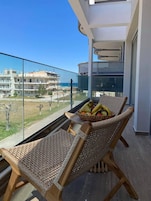 Varanda com cadeiras de vime, cesta de frutas e vista para prédios e o mar.