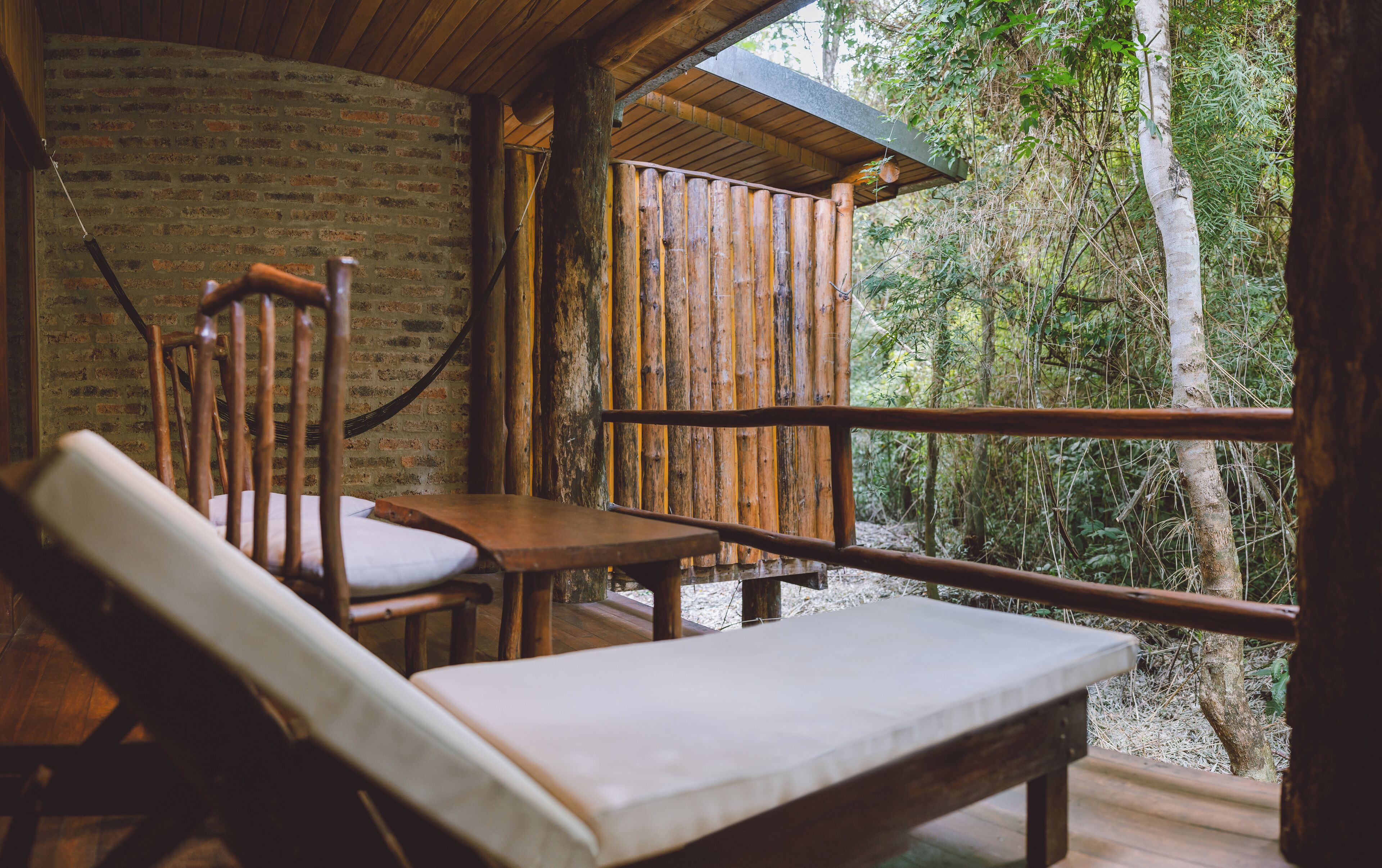 Um deck de madeira com um banco e uma mesa, com vista para uma área arborizada.