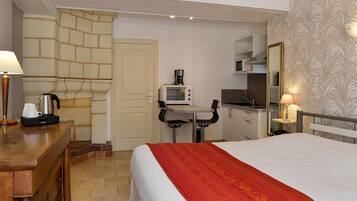 Quarto de hotel com uma cama, uma escrivaninha com cafeteira, micro-ondas e uma pequena mesa com cadeiras.