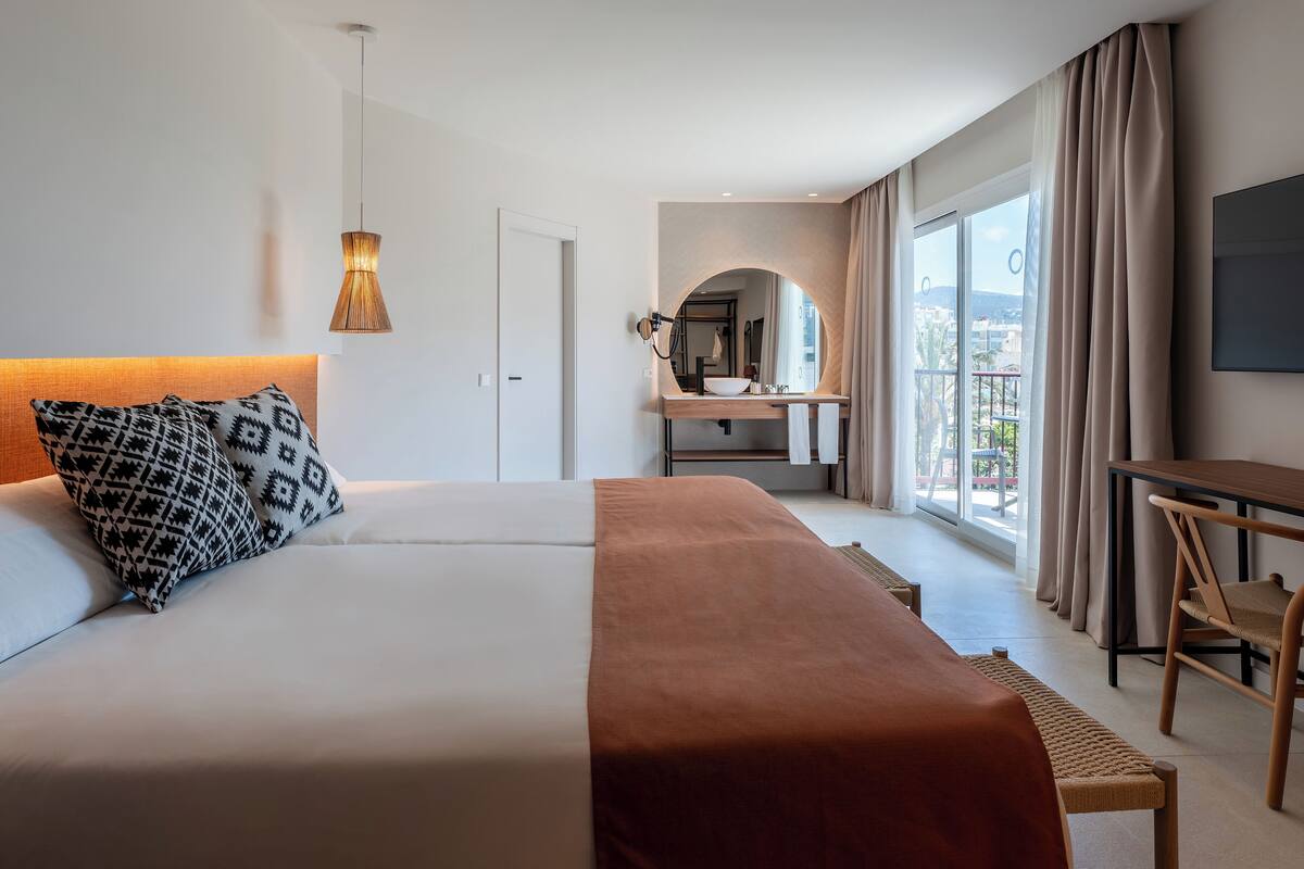 Quarto de hotel com uma cama grande, uma escrivaninha, uma cadeira, um espelho e vista para a cidade.