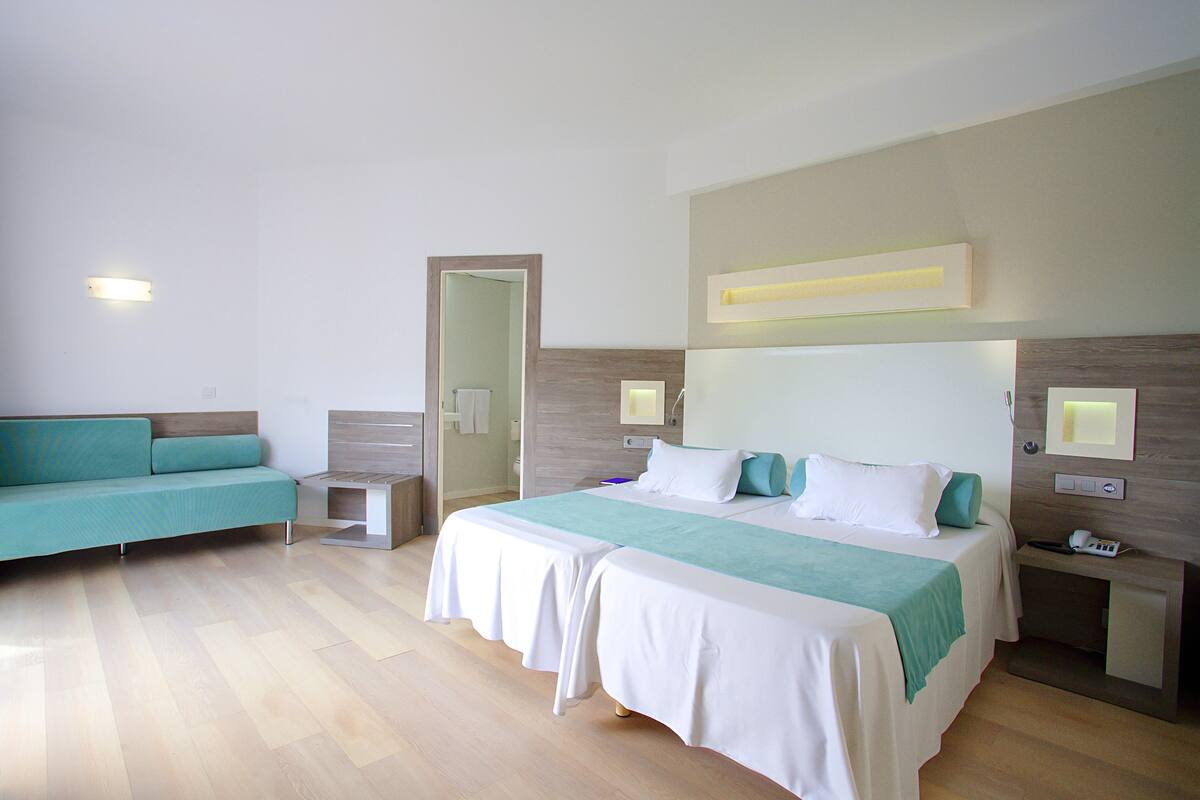 Quarto de hotel com uma cama grande, um sofá, uma mesinha de cabeceira e um espelho.