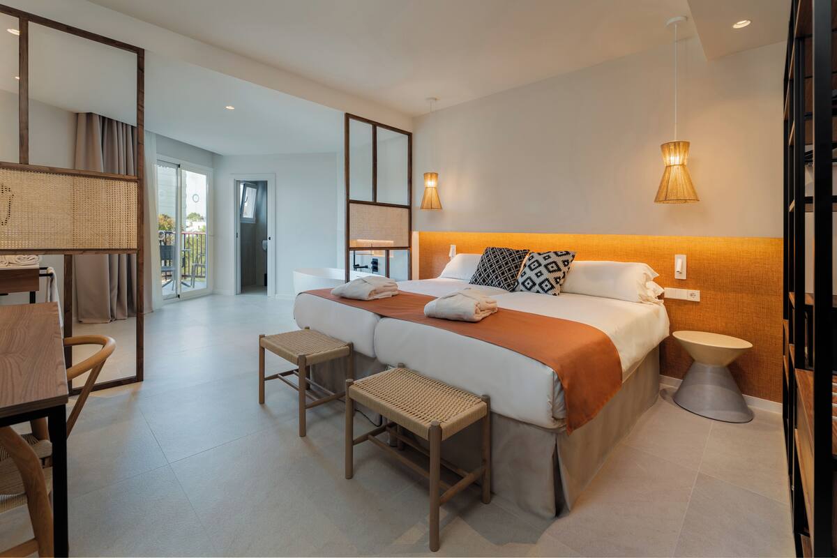 Quarto de hotel moderno com uma cama grande, duas mesas de cabeceira, uma escrivaninha e uma cadeira.