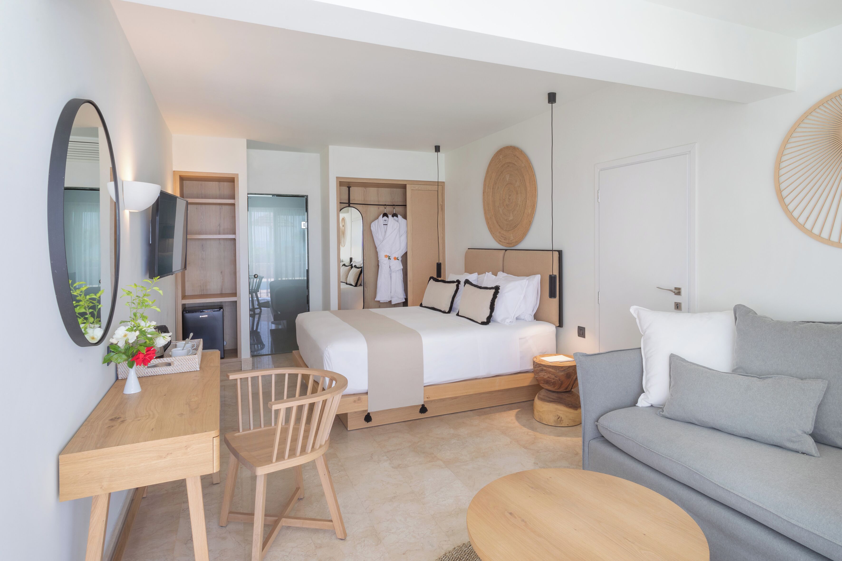 Quarto de hotel moderno com cama, sofá, escrivaninha com cadeira, espelho e decoração circular na parede.