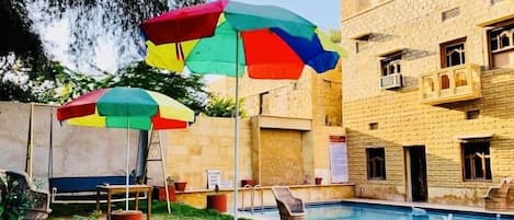 Uma piscina com borda de pedra, rodeada por uma área gramada e um edifício com fachada de pedra.