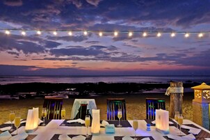 Mesa posta para dois com vista para a praia e oceano ao pôr do sol.