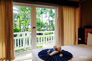 Quarto de hotel com uma cama, uma cadeira branca e vista para uma varanda com palmeiras.