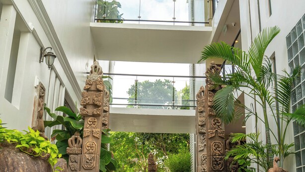 Um átrio de vários níveis com uma escadaria central, cercado por esculturas de pedra decorativas e plantas em vasos.
