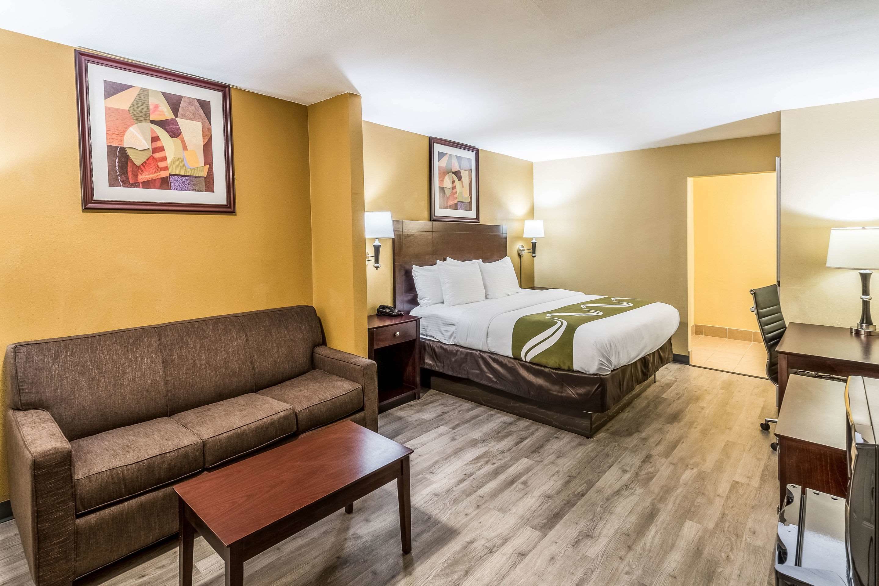 Quarto de hotel com cama, sofá, escrivaninha e duas luminárias.