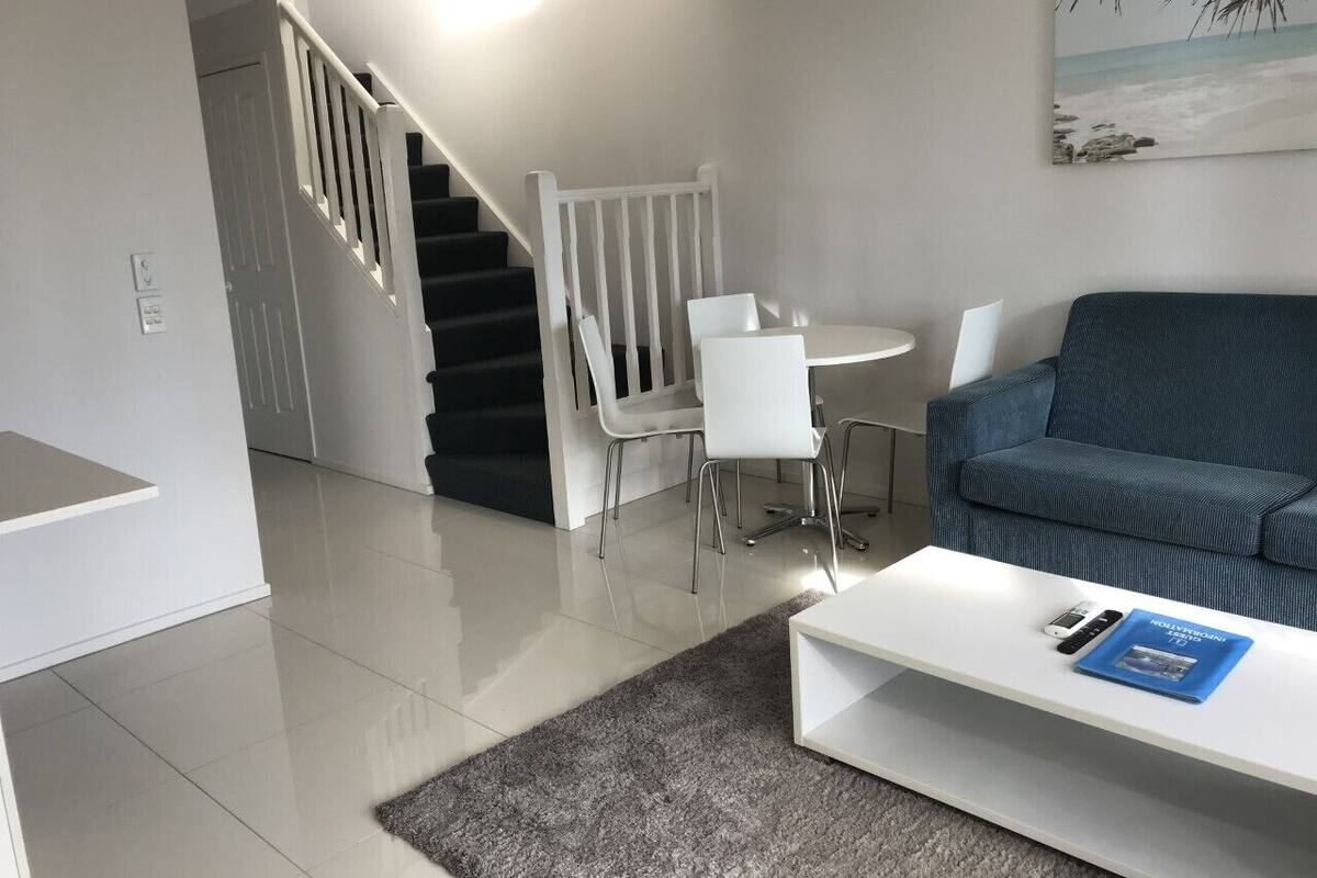 Uma sala de estar moderna com escada, móveis brancos e um sofá azul.