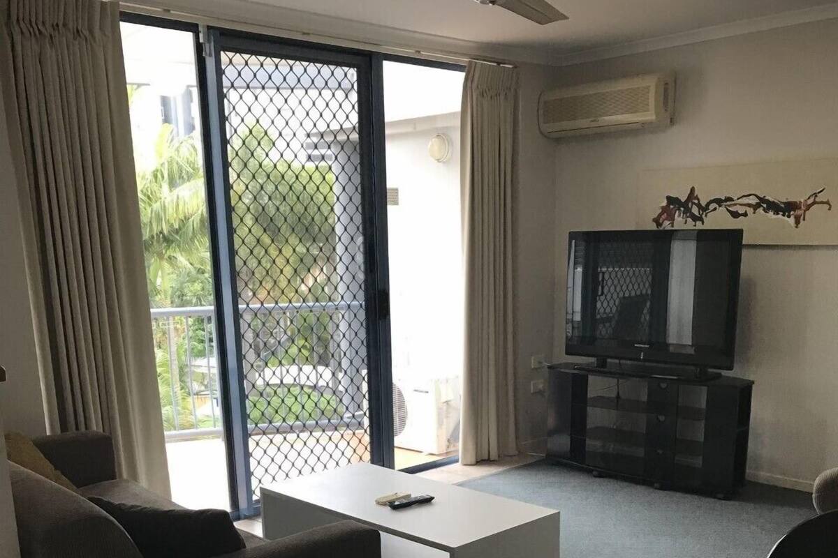 Uma sala de estar com sofá, mesa de centro, televisão em um suporte e ventilador de teto.