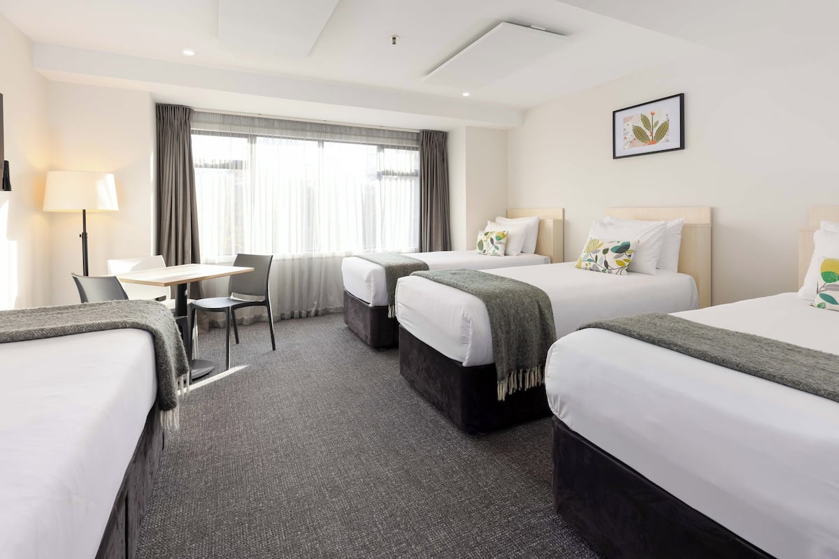 Quarto de hotel com duas camas de solteiro, uma escrivaninha, uma cadeira e uma janela com cortinas.