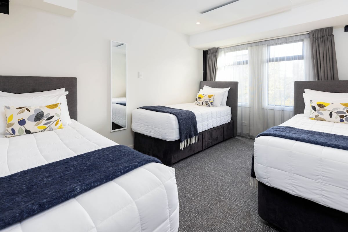 Quarto de hotel com duas camas, um espelho grande e uma janela com cortinas.