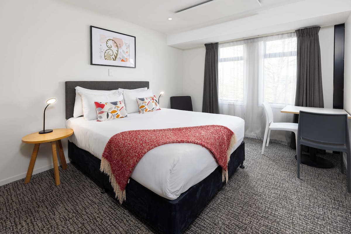 Quarto de hotel com uma cama grande, uma escrivaninha, uma cadeira e um quadro na parede.