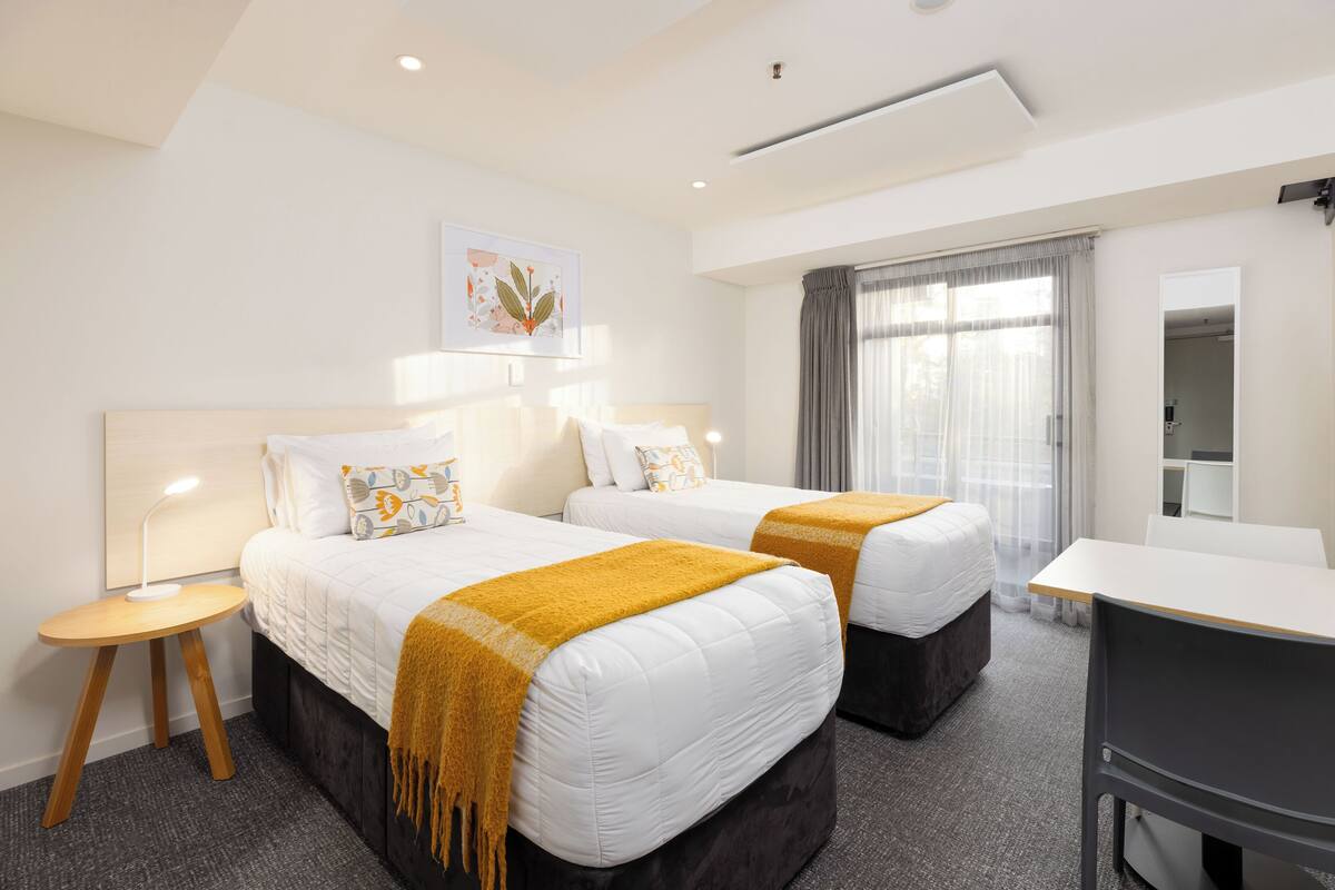 Quarto de hotel com duas camas, uma escrivaninha e um espelho.