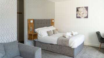 Quarto moderno com cama estofada cinza, sofá cinza e mesa de cabeceira de madeira.