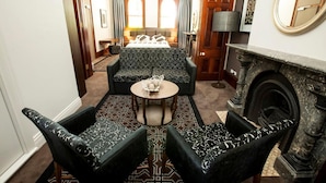 Quarto de hotel com uma cama, um sofá, duas poltronas, uma mesa redonda pequena e uma lareira.