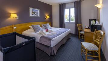 Quarto de hotel com cama, duas luminárias de cabeceira, escrivaninha com cadeira, janela com cortinas e um cesto de lixo.