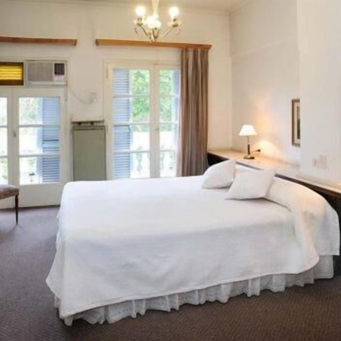 Quarto de hotel com cama, escrivaninha, cadeira, janela e porta.