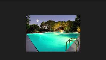 Piscina à noite com a lua no céu e árvores ao fundo.
