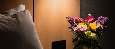 Quarto de hotel com cama, luminária na parede e um vaso de flores.