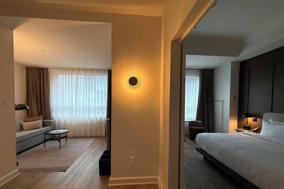 Quarto de hotel moderno com sofá, uma mesinha, cama e luminária circular na parede.