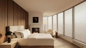Quarto moderno com cama grande, lareira, sofá e vista para o exterior através de amplas janelas.