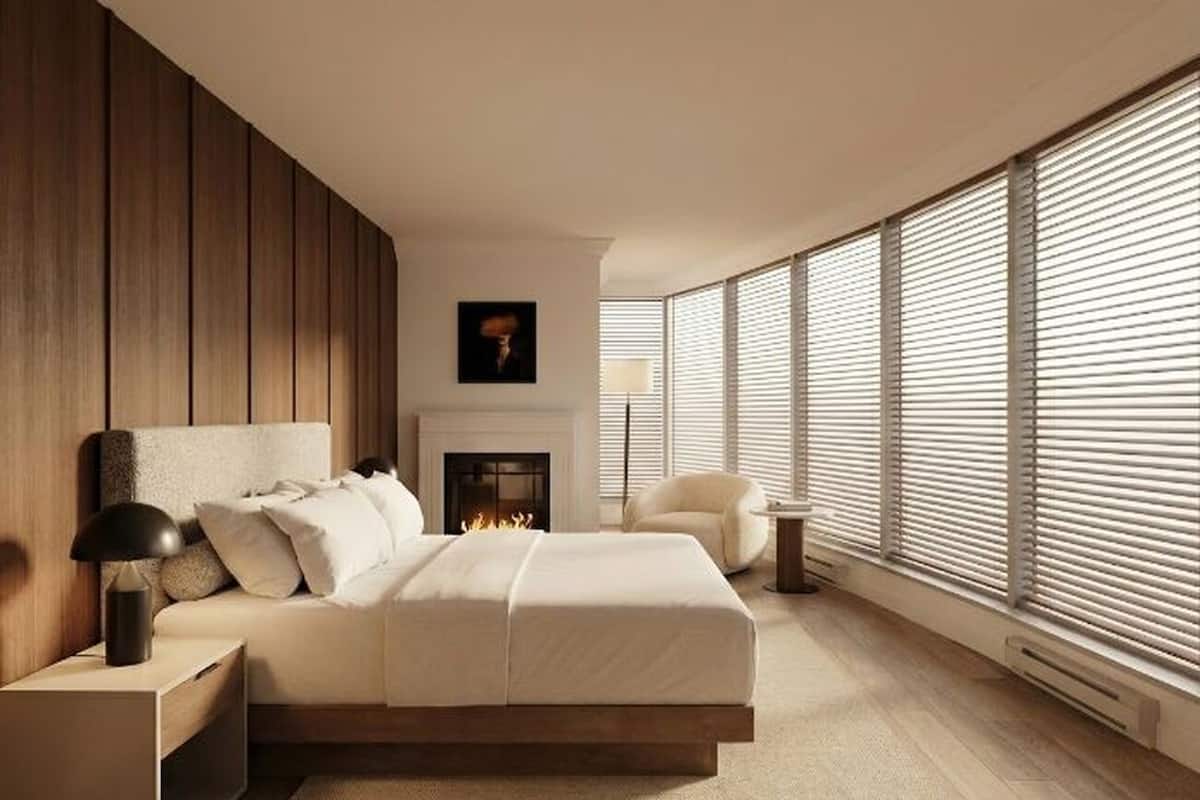 Quarto moderno com cama grande, lareira, sofá e vista para o exterior através de amplas janelas.
