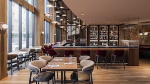 Restaurante moderno com área de bar, janelas amplas e diversas opções de assento.