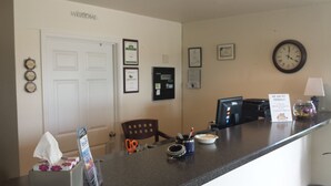 Bancada de recepção com placa de 'Welcome', relógio, certificados emoldurados e placa indicando que aceita animais de estimação.