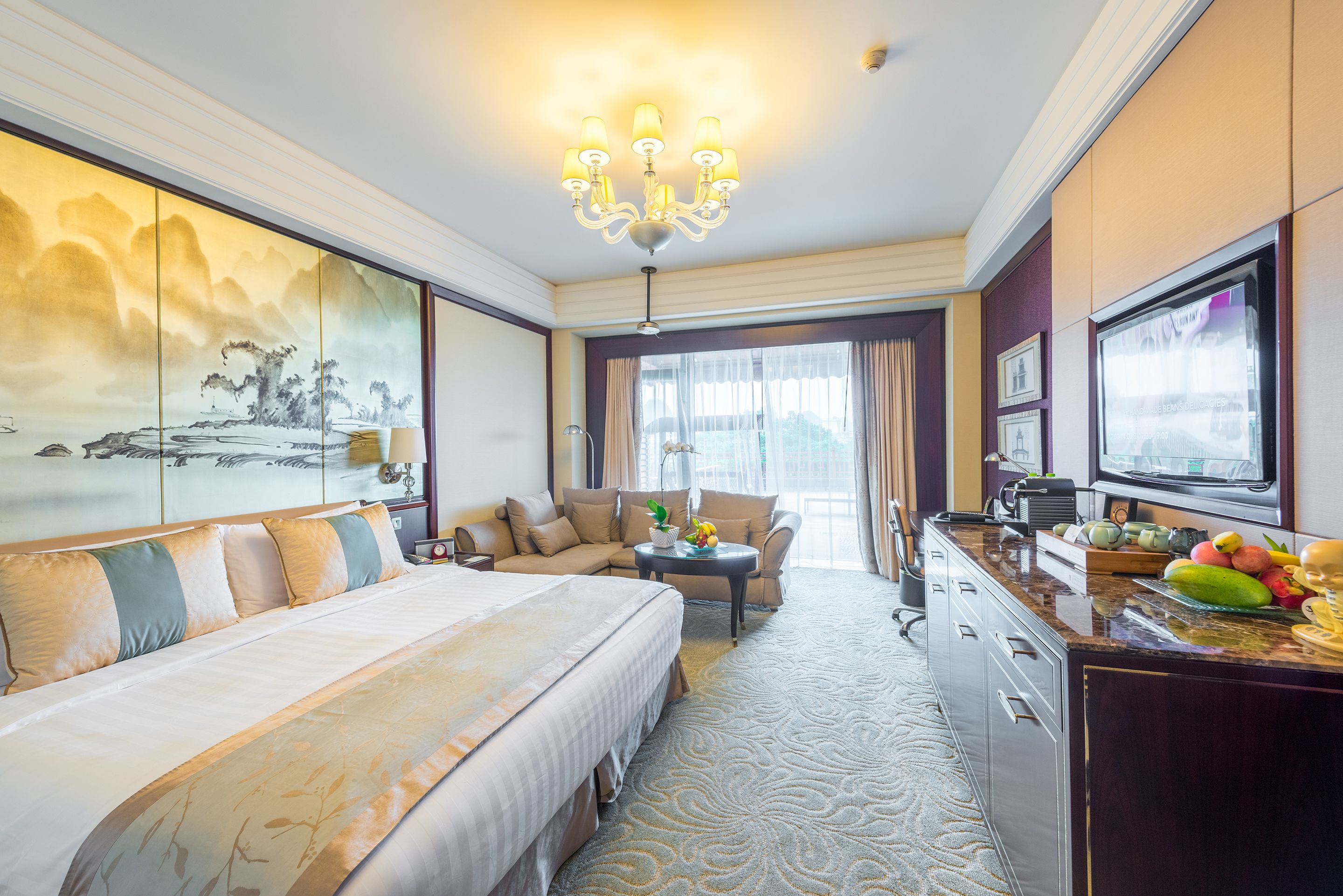 Quarto de hotel com uma cama grande, um sofá, área de refeições e vista para o exterior.