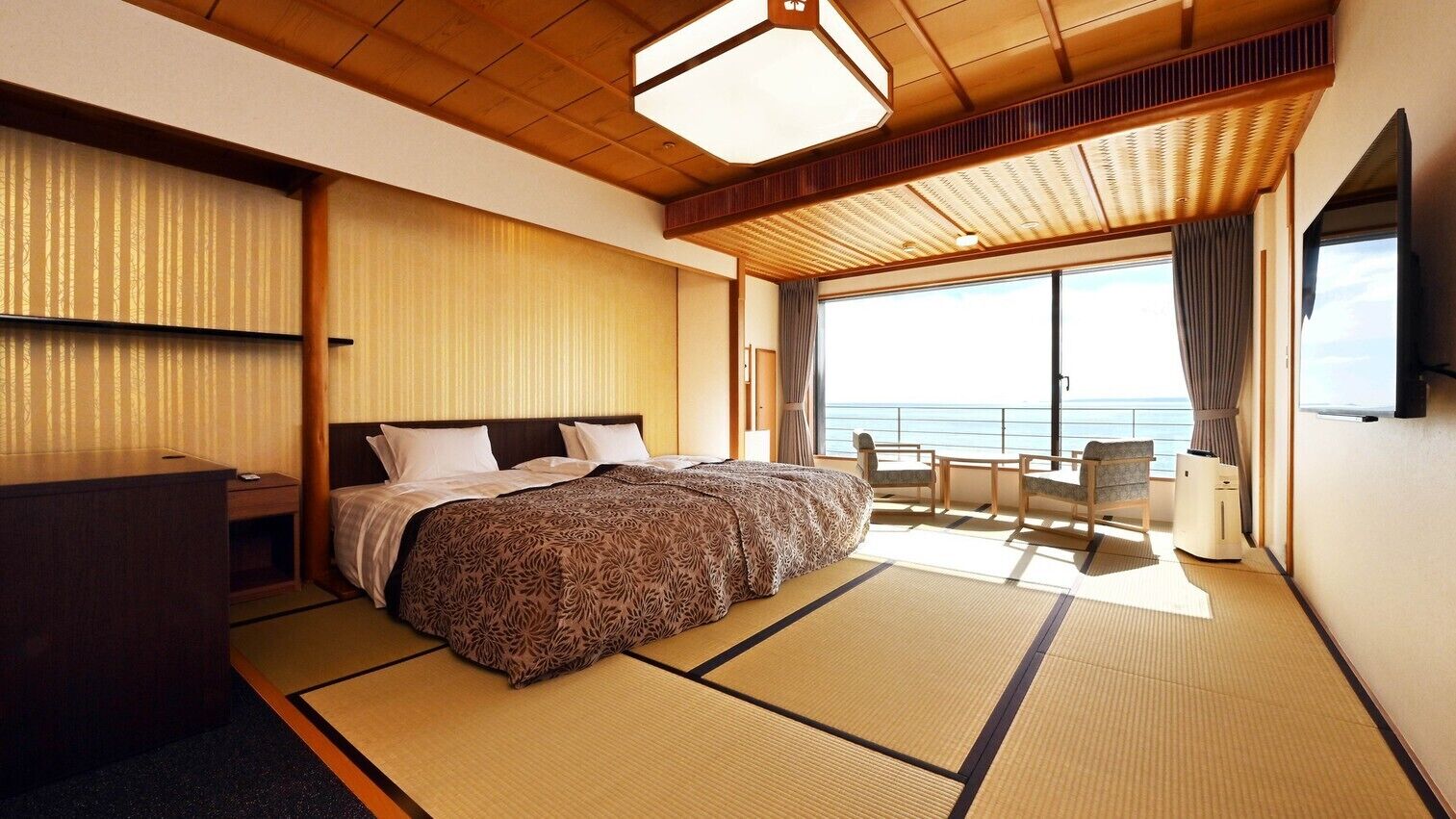 Quarto com cama, escrivaninha, cadeira e vista para o mar.