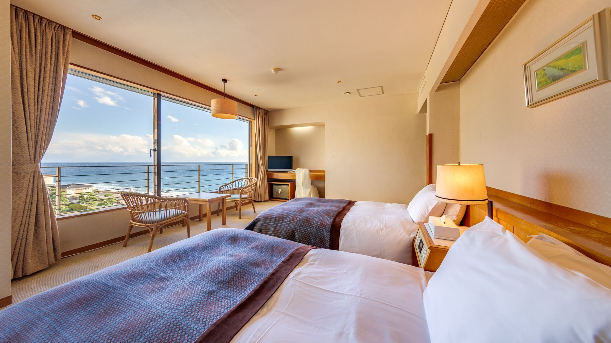 Quarto de hotel com duas camas, televisão, escrivaninha e vista para o oceano.