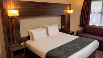 Quarto de hotel com cama grande, duas mesas de cabeceira, um sofá e janela com cortinas.