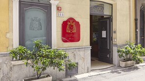 Fachada de edifício com uma grande entrada arqueada, uma placa vermelha com um brasão e duas plantas em vasos.