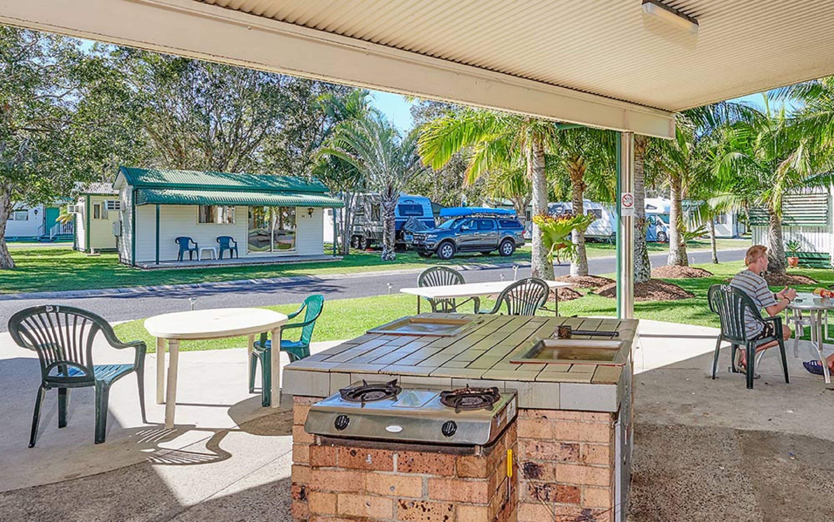 Um pátio externo com churrasqueira de tijolos, cadeiras verdes e uma mesa.